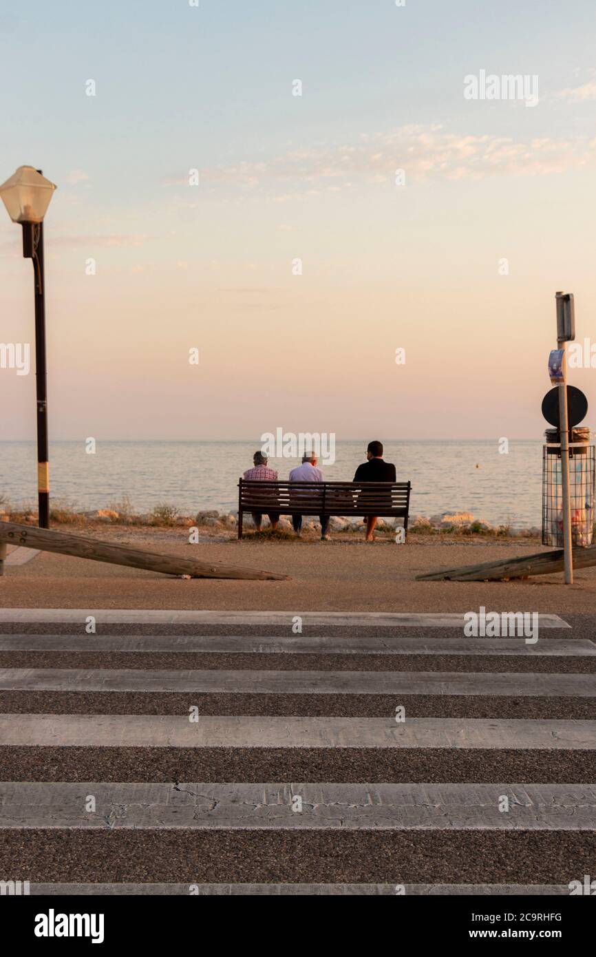 three men from behind sitting on a Bench chat while looking out to see ...