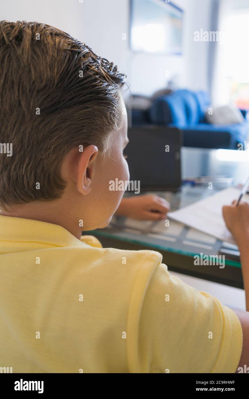 Back view of young boy doing schoolwork at home on dining room table ...