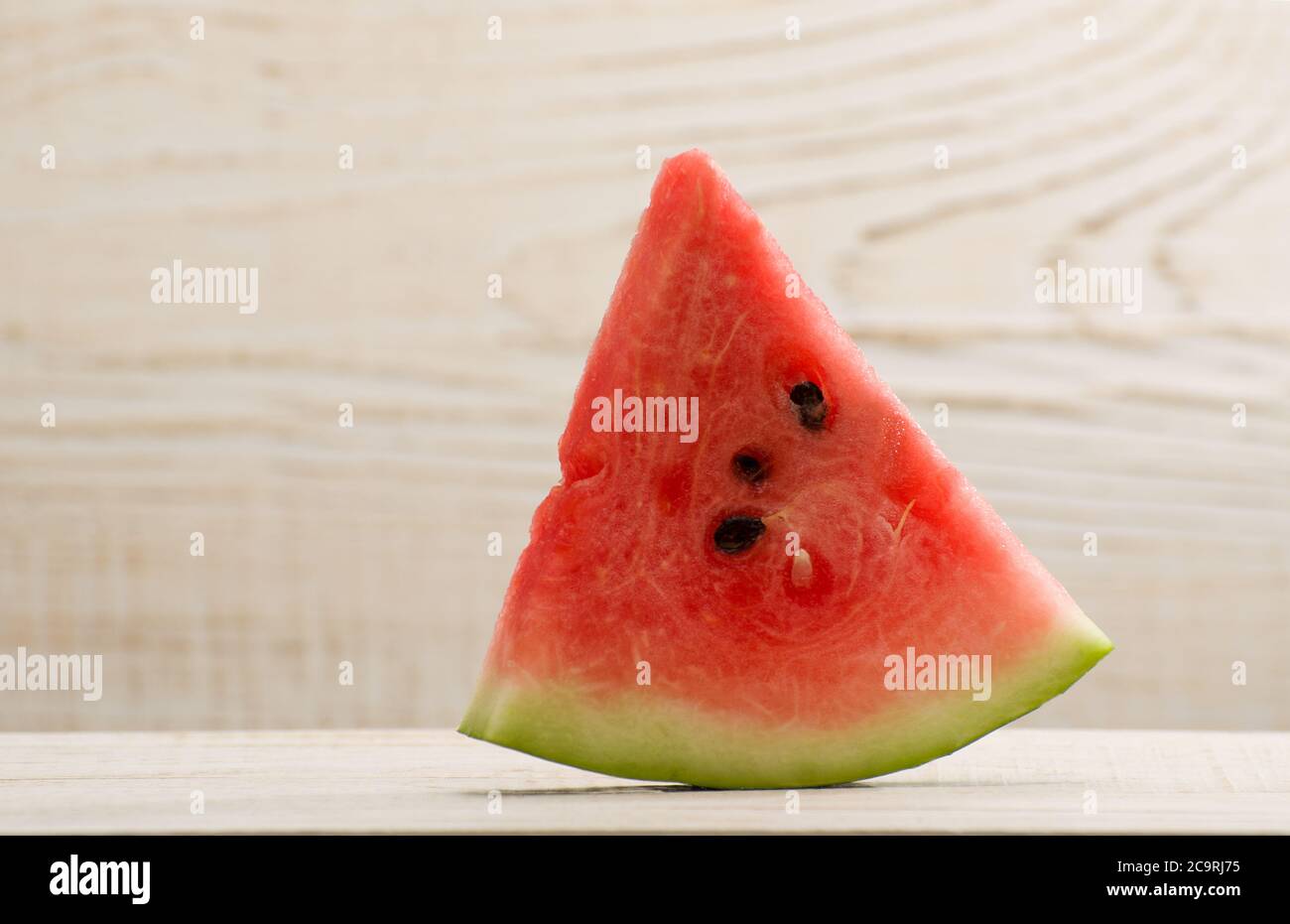 Triangular watermelon slice on a light wooden background Stock Photo ...