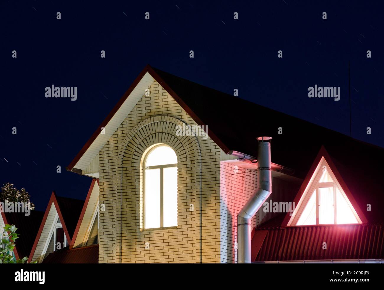 Light at the night arched window on the top floor, the pink light of ...