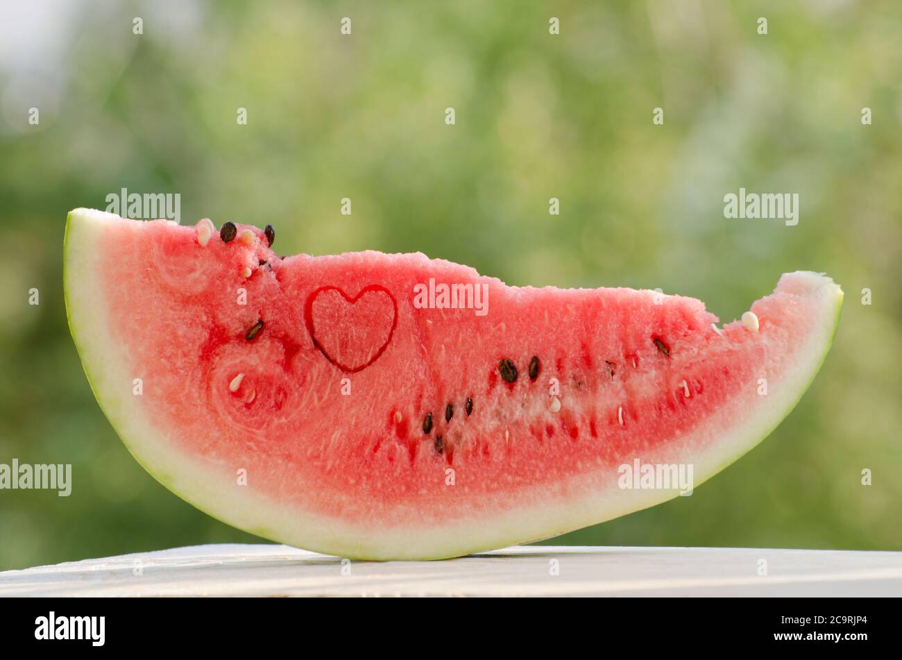 Large slice of watermelon on a green background with a heart in the ...
