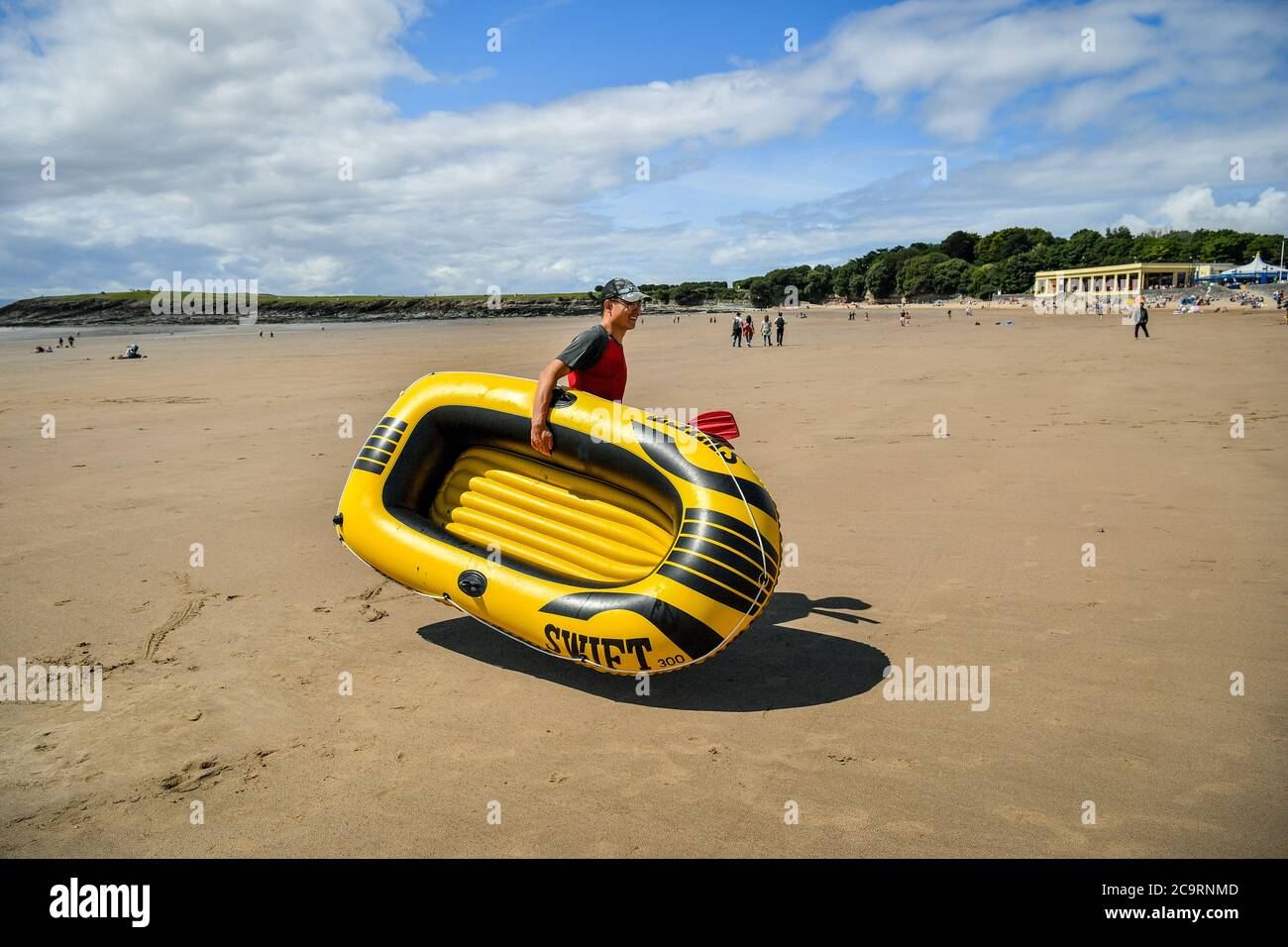 A man carrying an inflatable dinghy on Barry Island beach, Wales, as ...