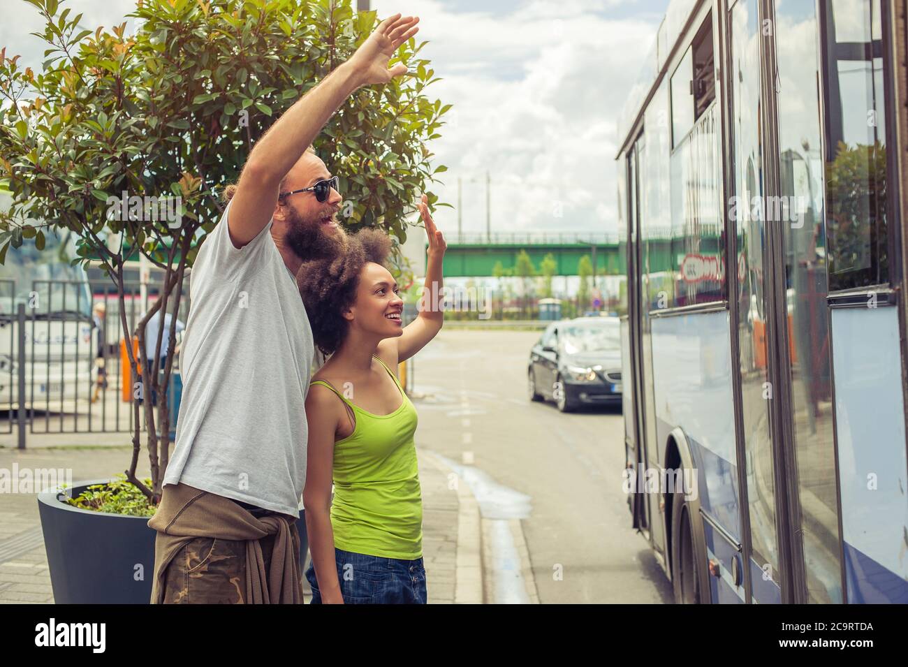 Young couple waving goodbye to their friends on the bus at bus station ...