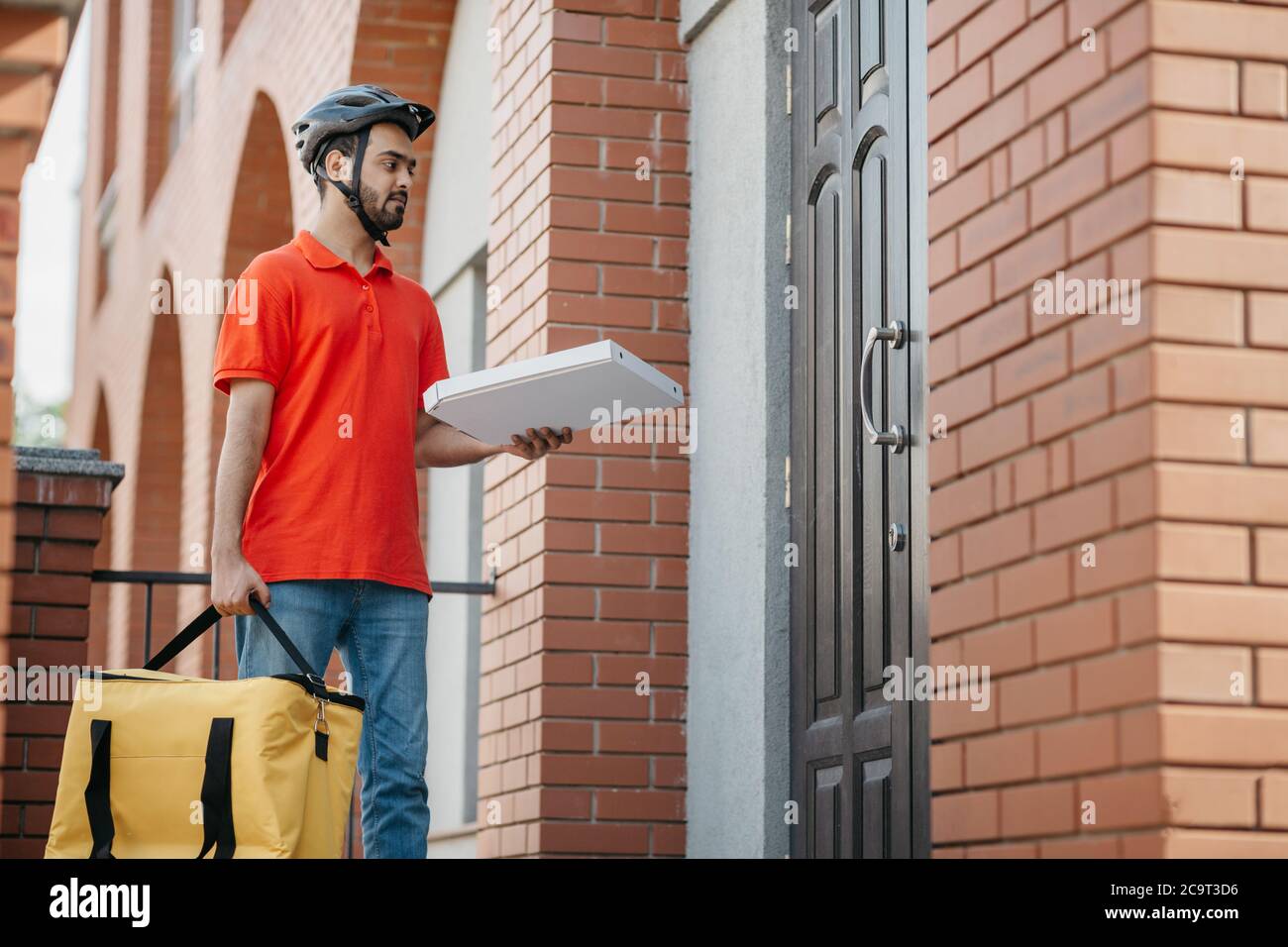Courier delivers pizza to door. Young deliveryman with safety helmet ...