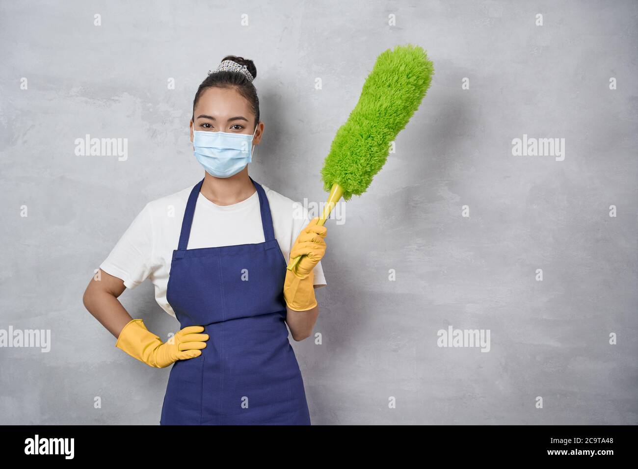Young woman, cleaning lady in uniform wearing medical mask holding ...