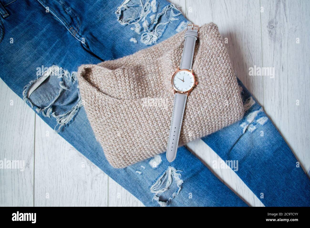 Stylish clock on a sweater and torn jeans. Fashionable concept, wooden ...