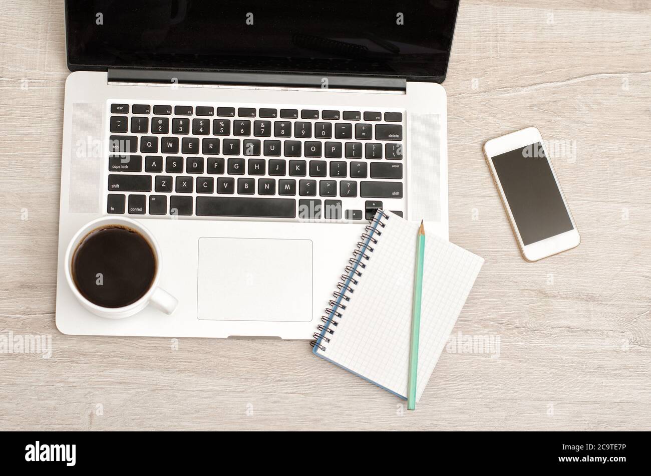 Mug of coffee and a notebook on an open laptop, smartphone. Light wood ...