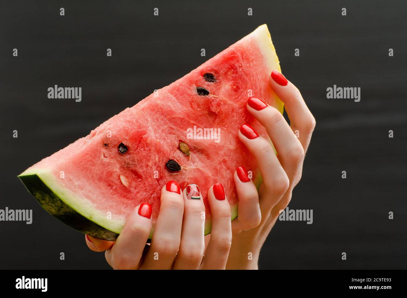 Large slice of ripe watermelon in female hands on a black background ...