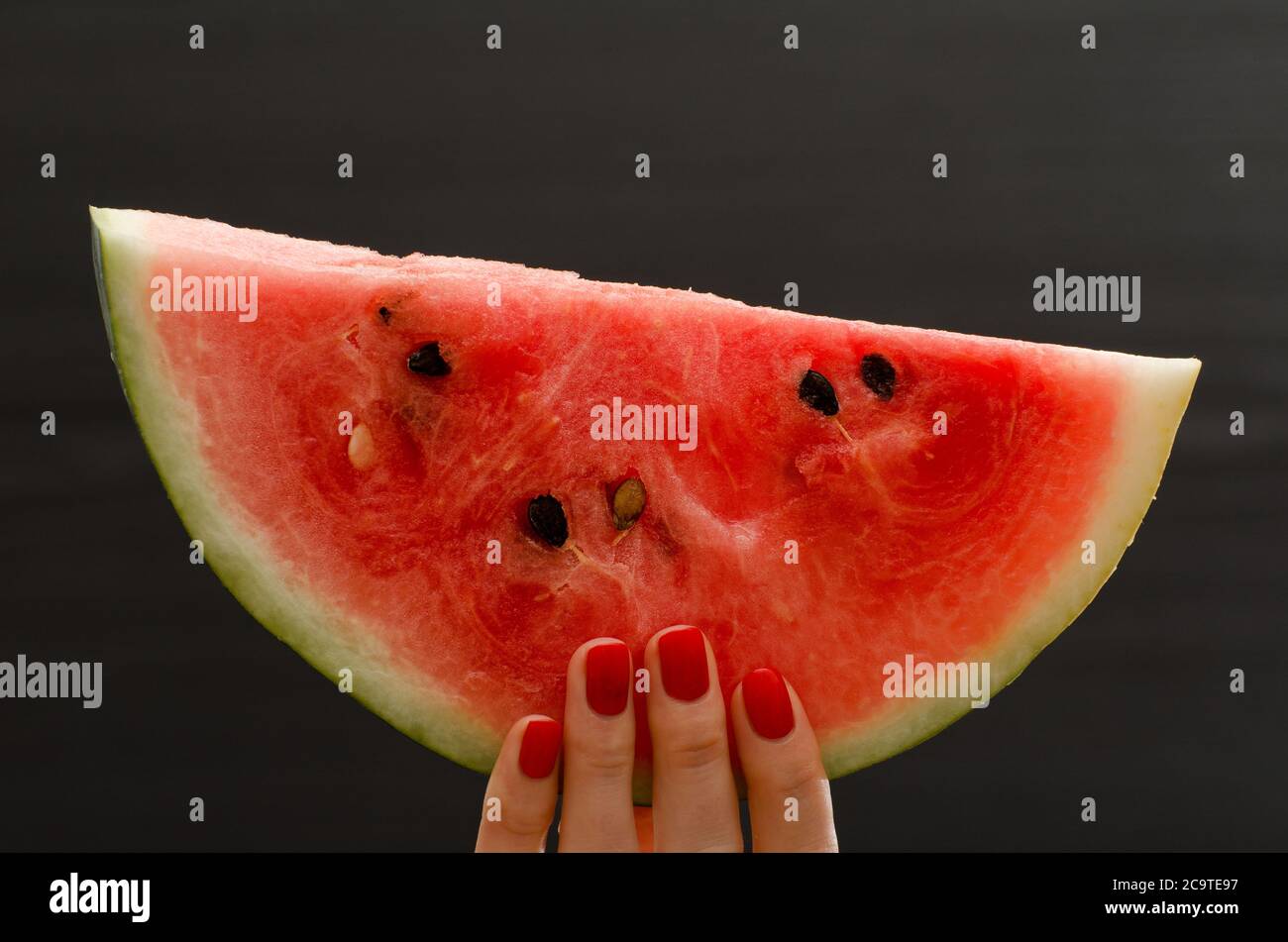 Semicircle of ripe watermelon in female hands on a black background ...