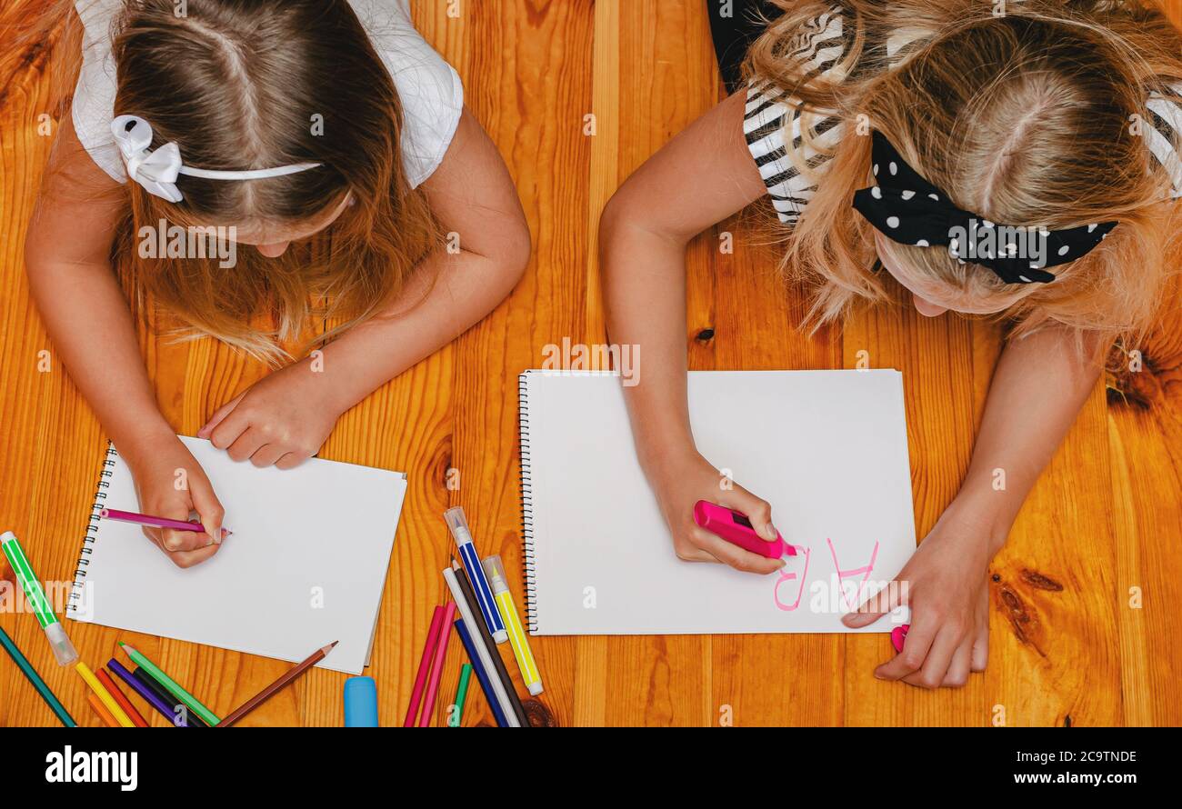 Two caucasian girls having fun on the floor, drawing and writing ...