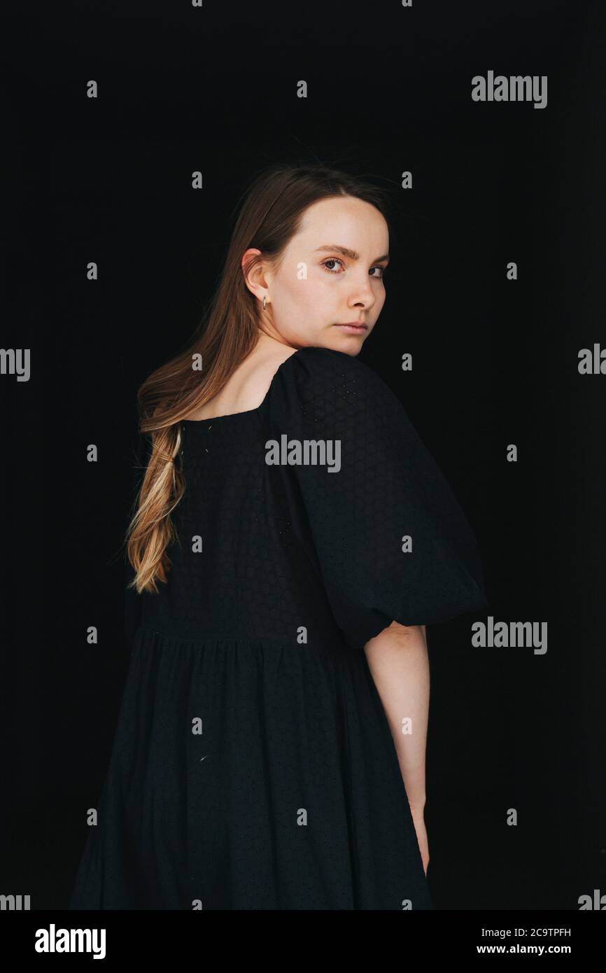 Woman looking at the camera over her shoulder. In black dress over ...