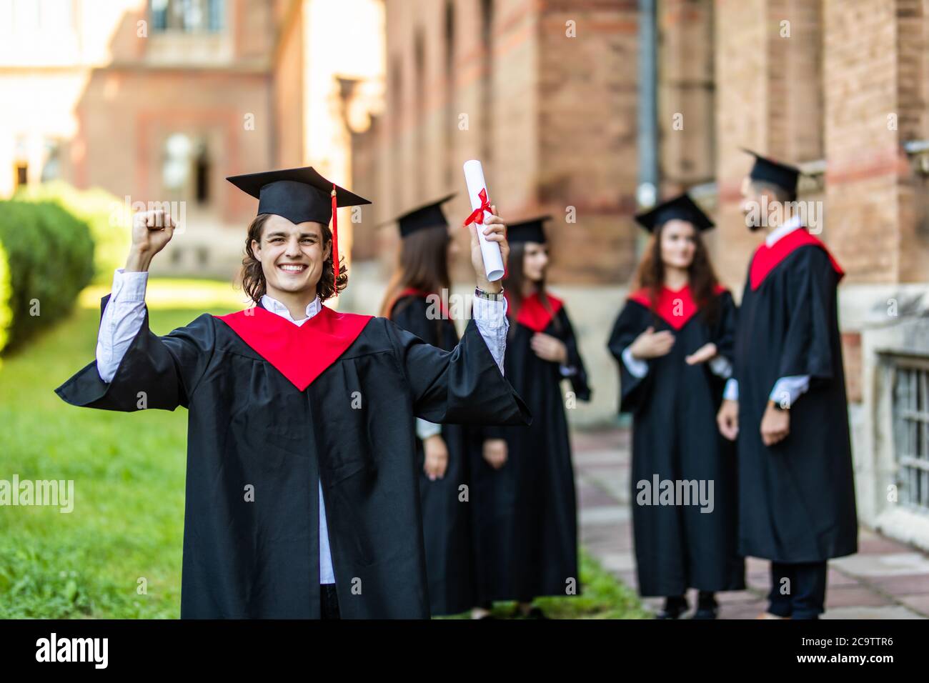 Close-up of a smiling graduate smiling with her friends in background ...