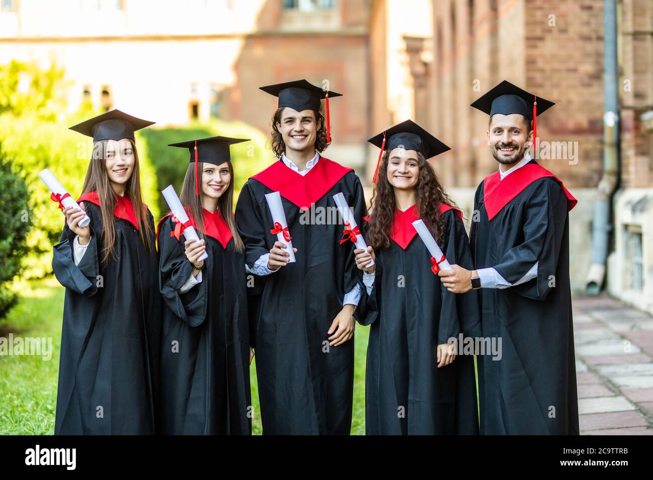 Happy graduates. Five college graduates standing in a row and smiling ...