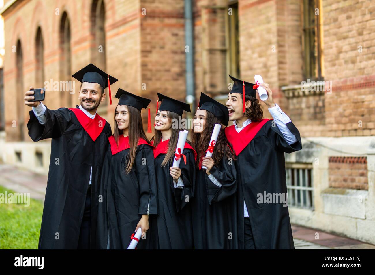 Four college graduates in graduation gowns standing close to each other ...