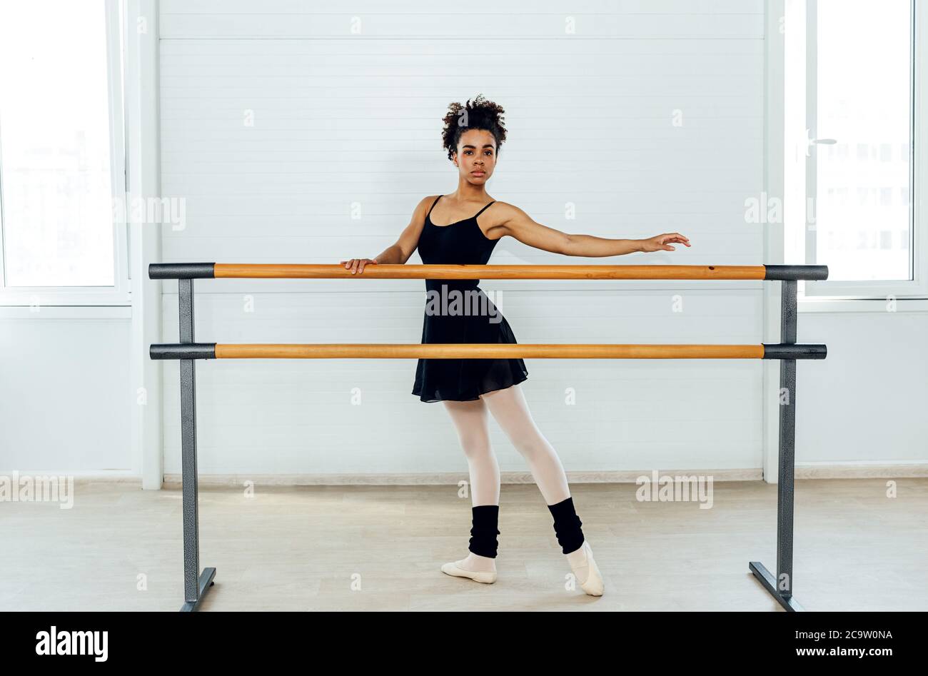 Female ballet dancer with curly hair holding a barre preparing for a ...