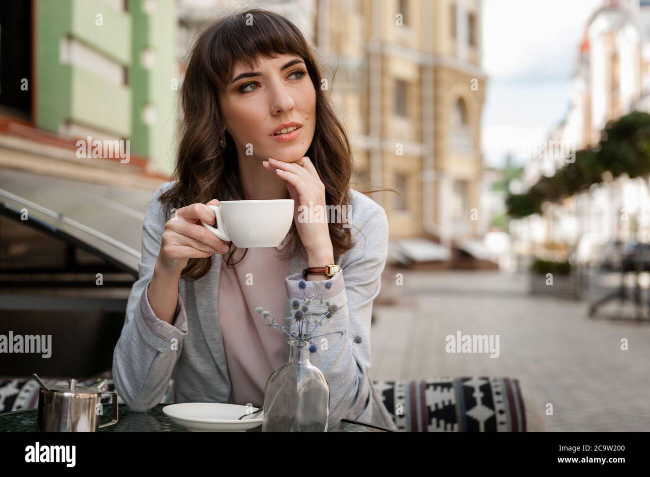 a girl sits outside in a coffee shop with a cup of coffee. Young woman ...