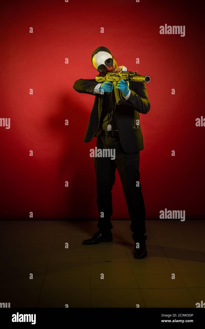 Actor man in a mask with a weapon in his hands posing on a red ...