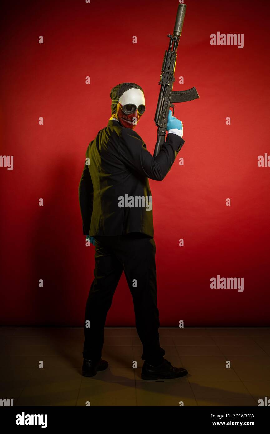 Actor man in a mask with a weapon in his hands posing on a red ...