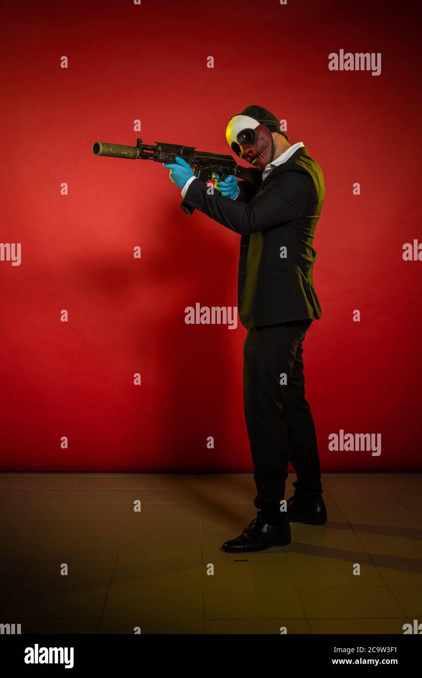 Actor man in a mask with a weapon in his hands posing on a red ...