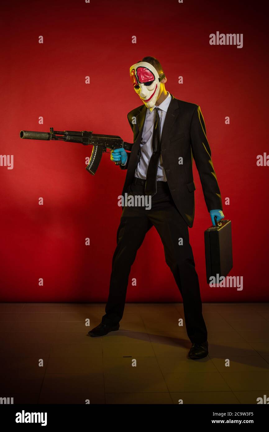 Actor man in a mask with a weapon in his hands posing on a red ...