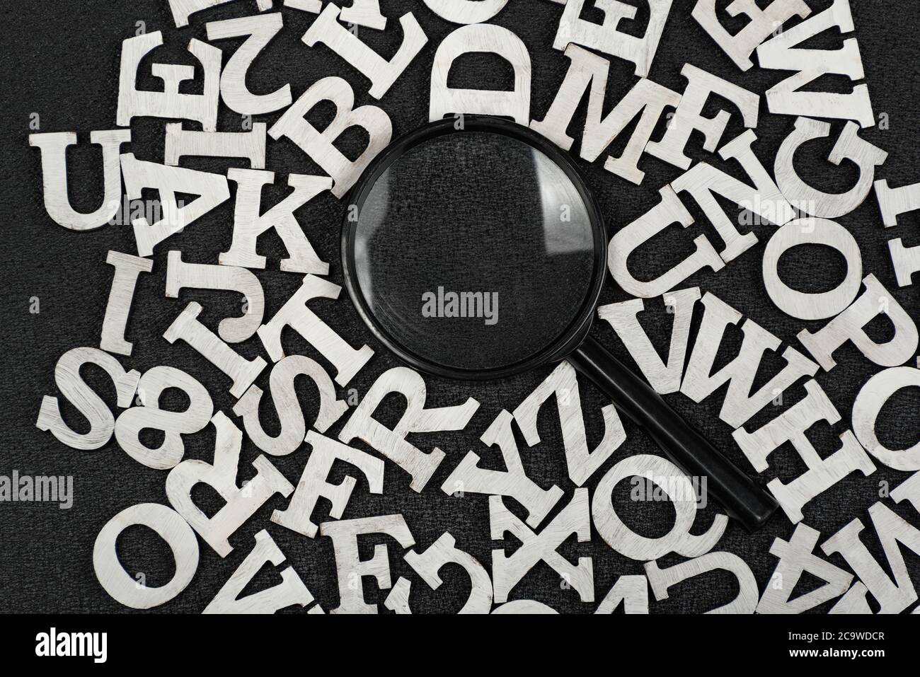 Magnifying glass surrounded by letters of English alphabet on black ...