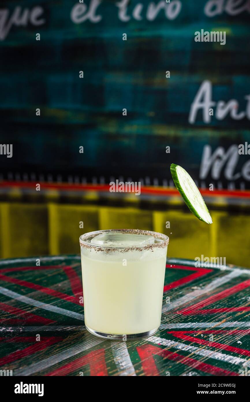A slice of cucumber falling into a cocktail in a rocks lowball glass ...