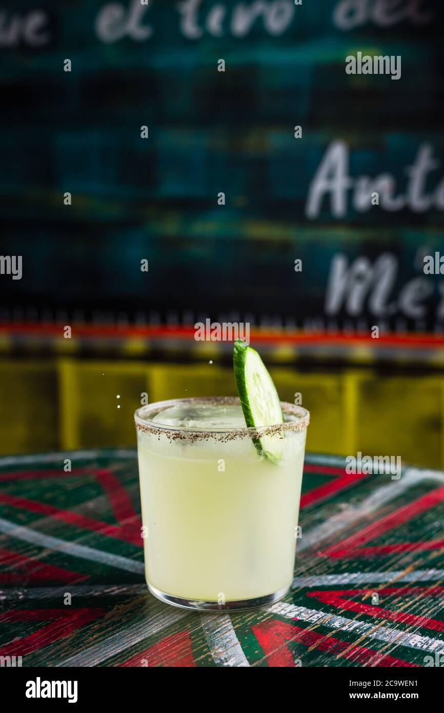 A slice of cucumber falling into a cocktail in a rocks lowball glass ...