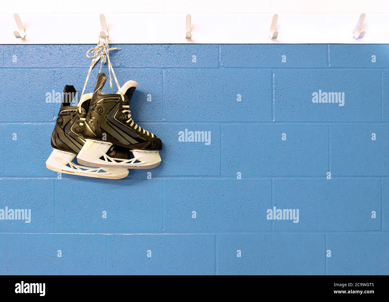 Hockey skates hanging over blue pastel wall in locker room with copy ...