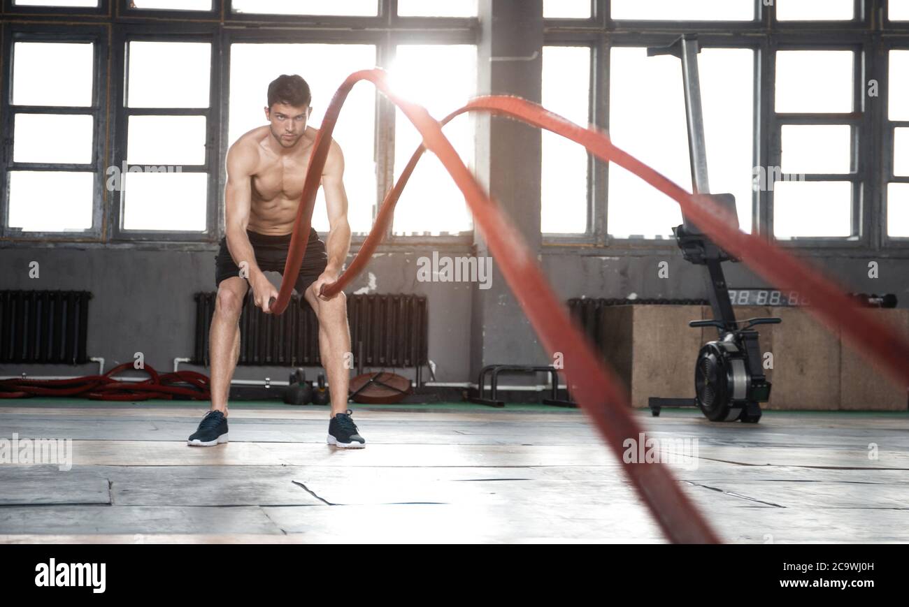 Athletic young man with battle rope doing exercise in functional ...