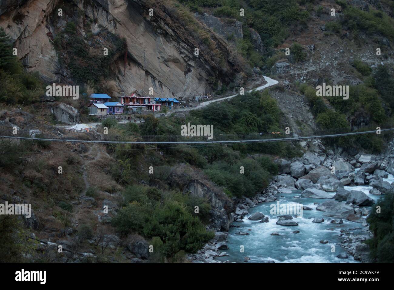 Nepalese mountain village by a suspension bridge over the Marshyangdi ...