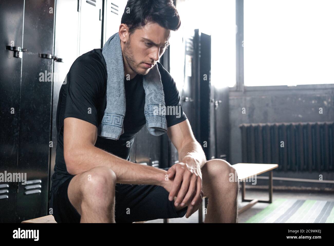 Young athletic Caucasian man sitting alone in dark gym locker room ...