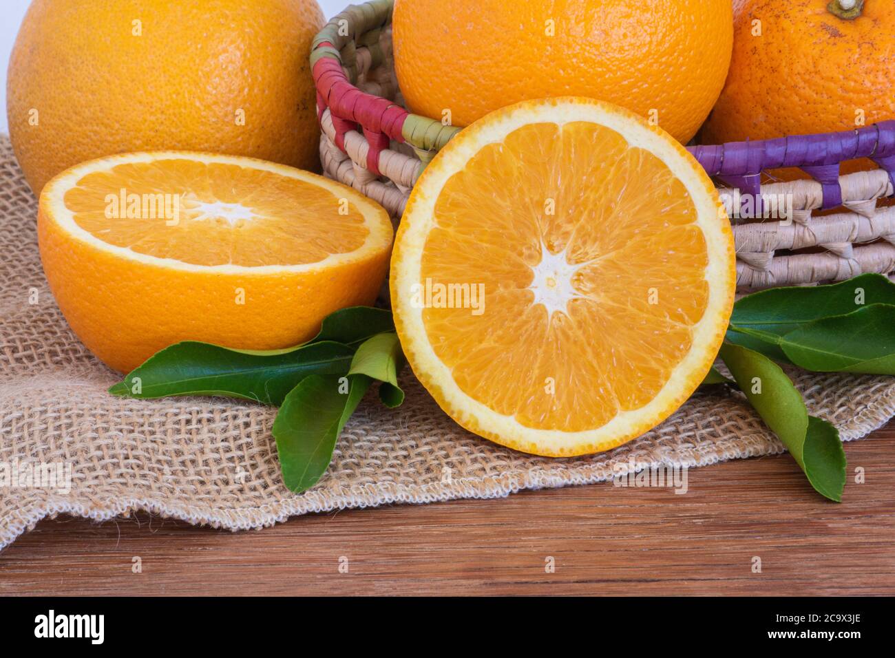 Whole ripe oranges and pieces cut in half with green leaves. Close-up ...
