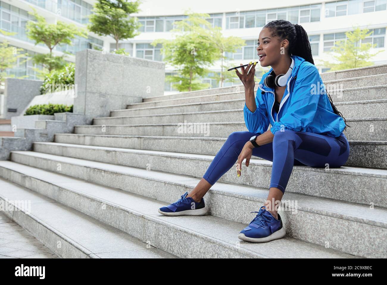 Pretty fit mixed-race young sportswoman sitting on steps and recording ...