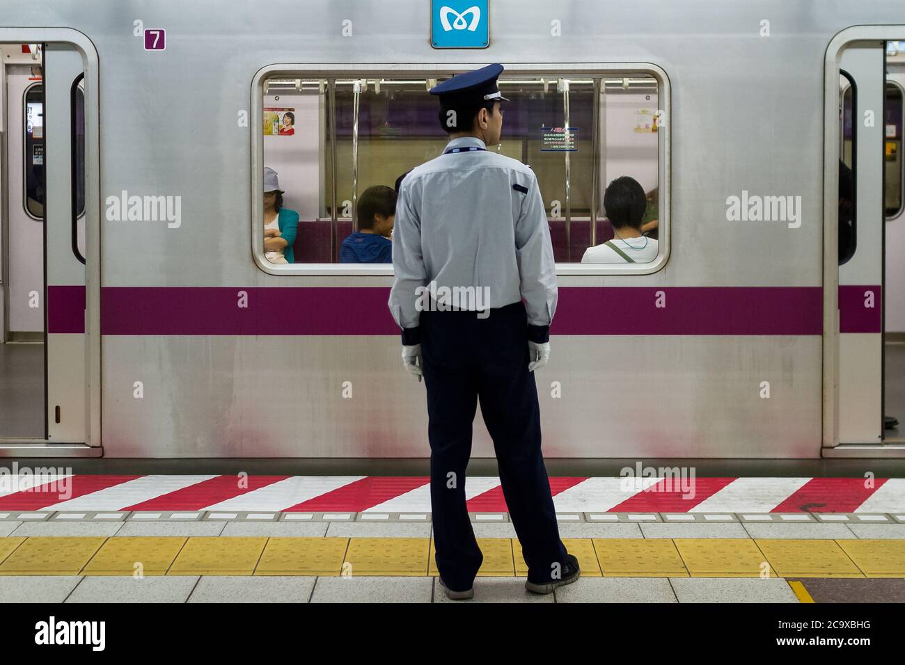 A train guard on a platform at Jinbocho station as a Hanzomon Line ...