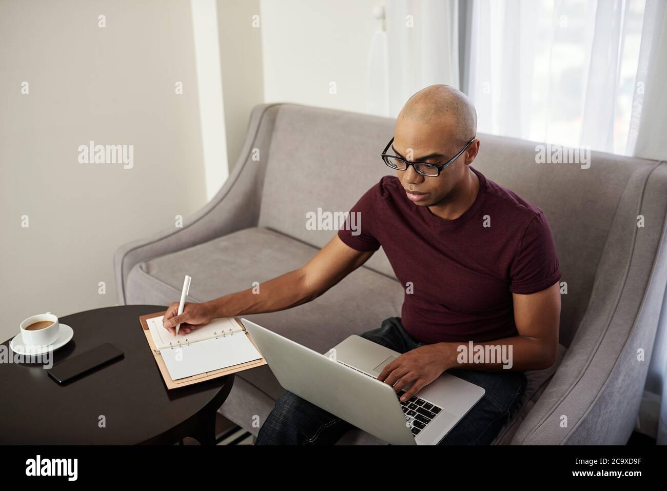 Handsome young man watching webinar of laptop screen and taking note in ...