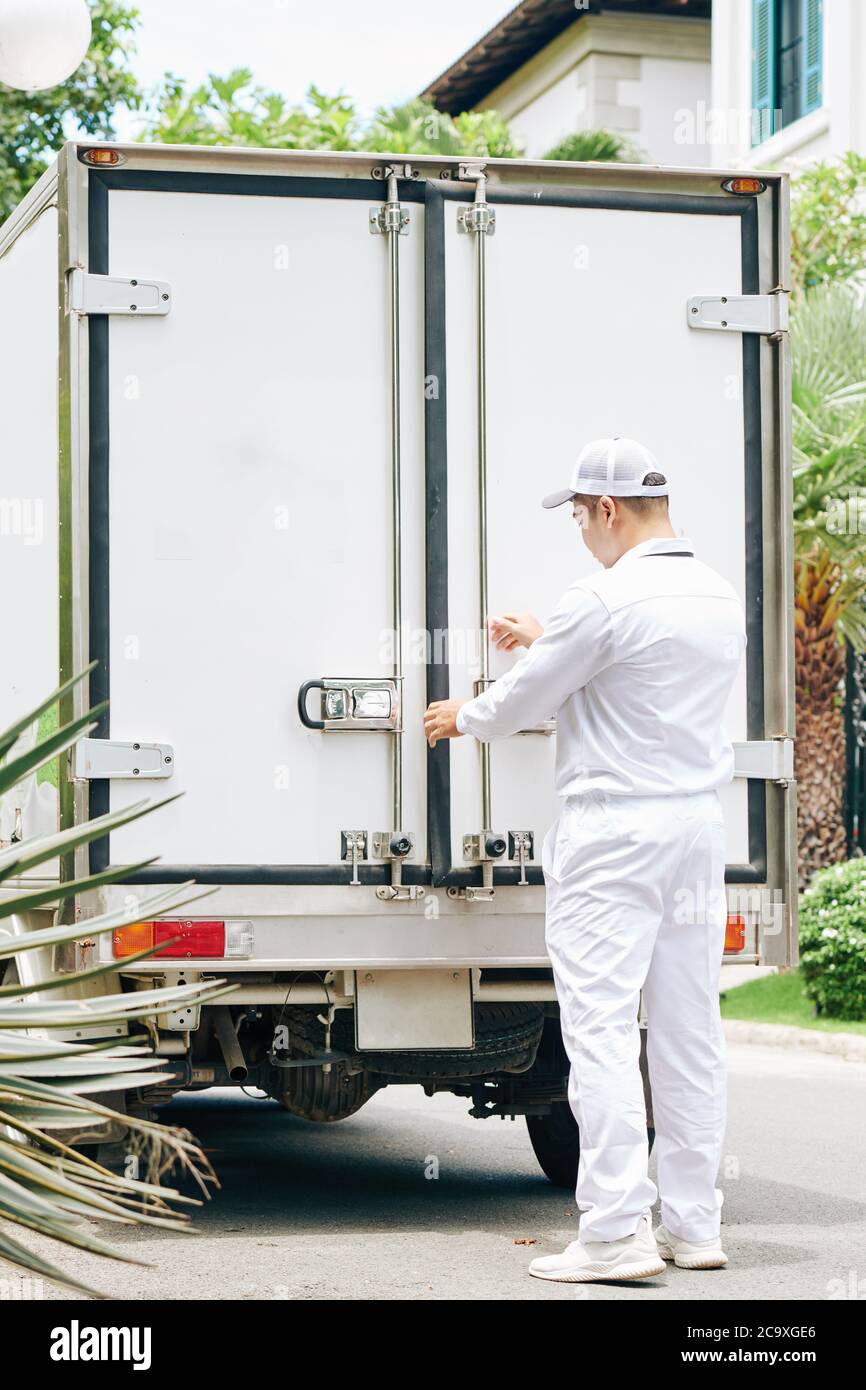 Delivery man in white uniform closing doors of van trunk after loading ...