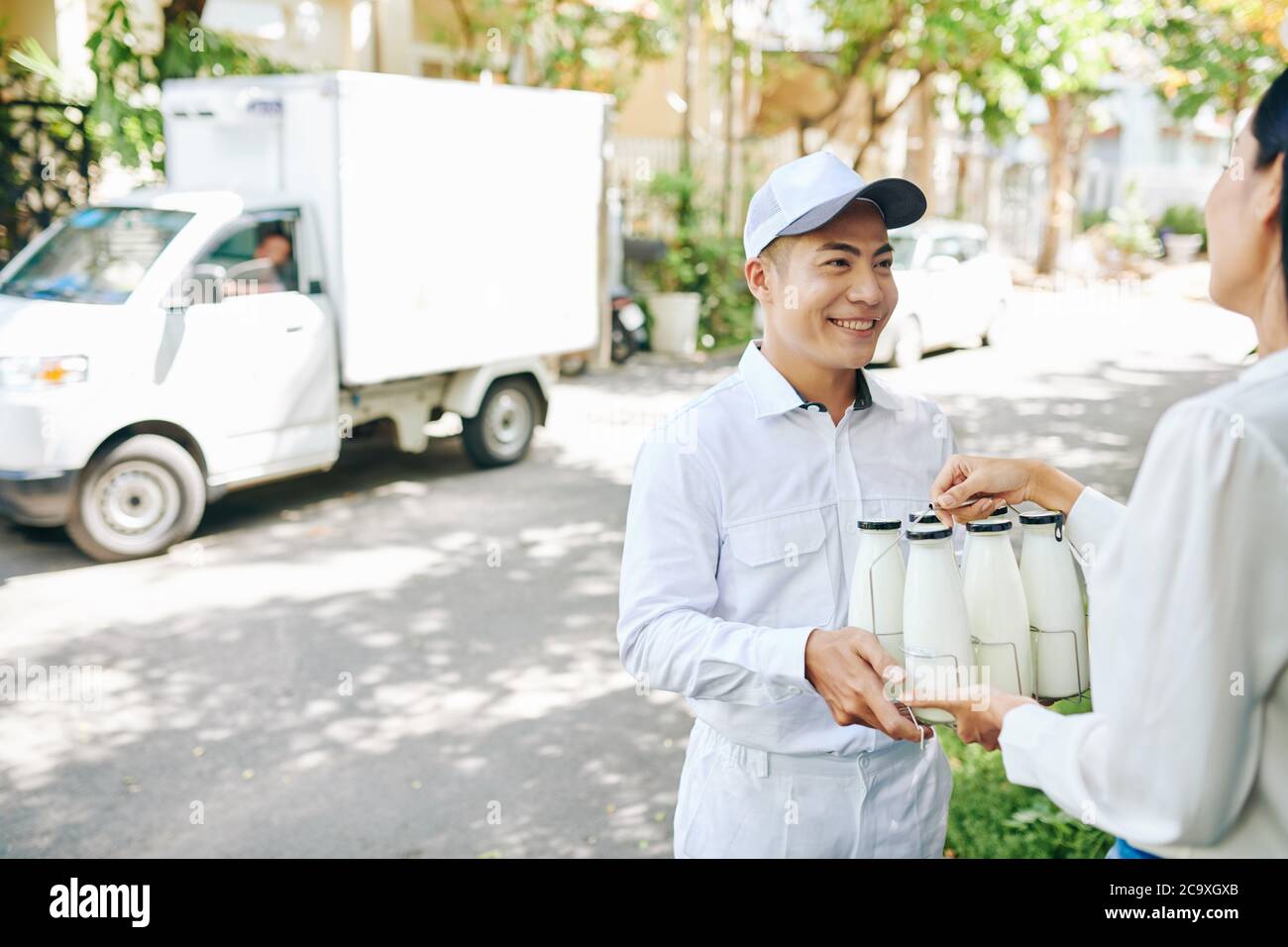 Smiling milkman deliverying milk bottles to pretty female customer ...