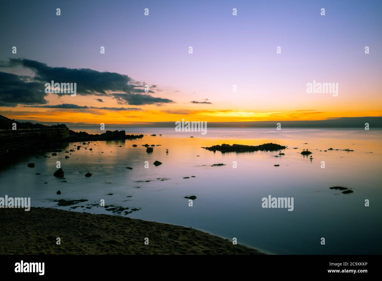 Calm bay water with rocks silhouettes at dusk Stock Photo - Alamy