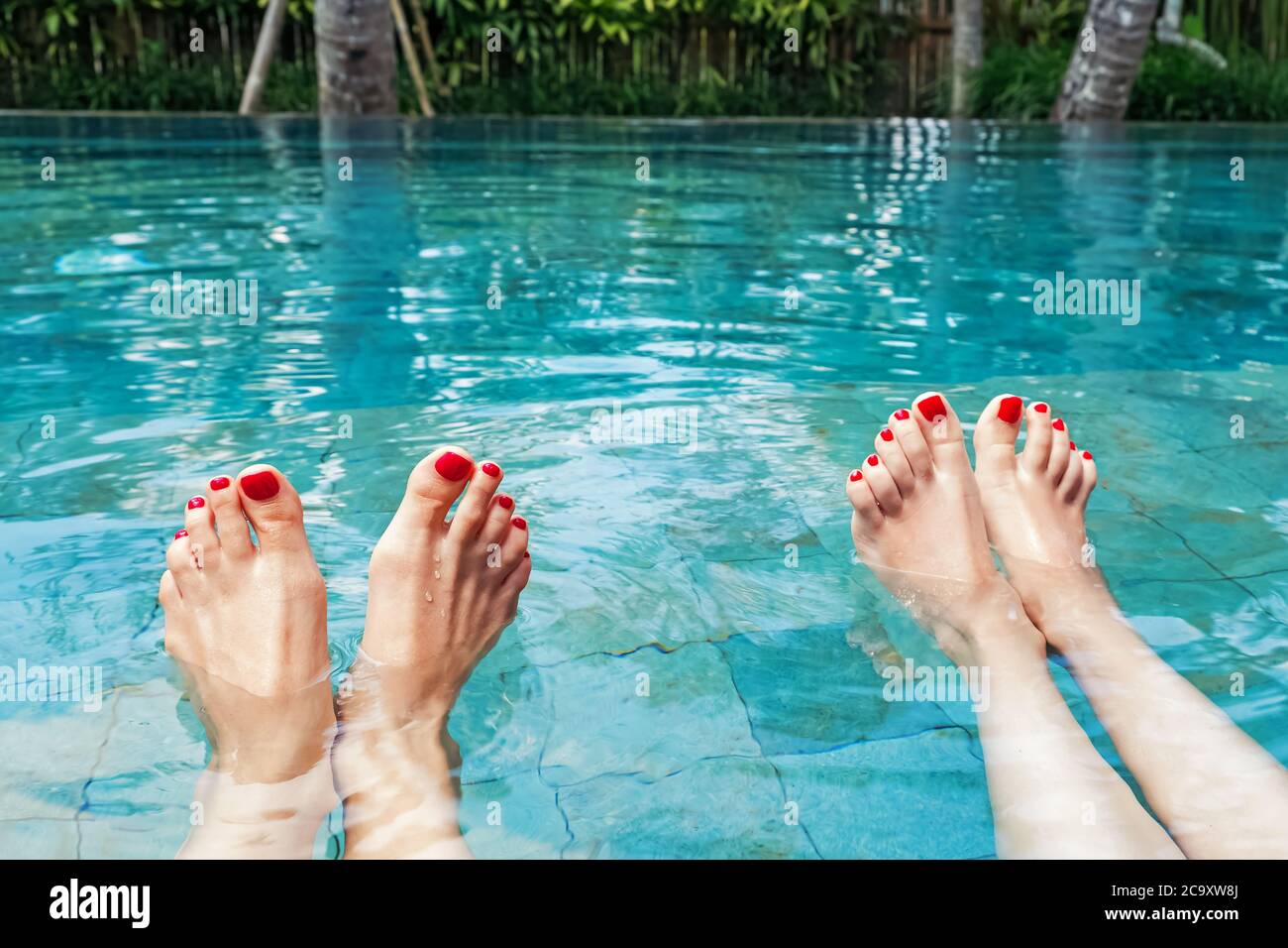 Girls sit on the edge of swimming pool with their feet in the water ...