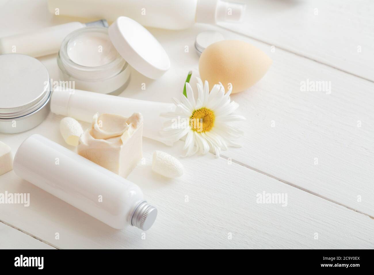 Set white cosmetic products on wooden table with flowers. Beauty sponge ...