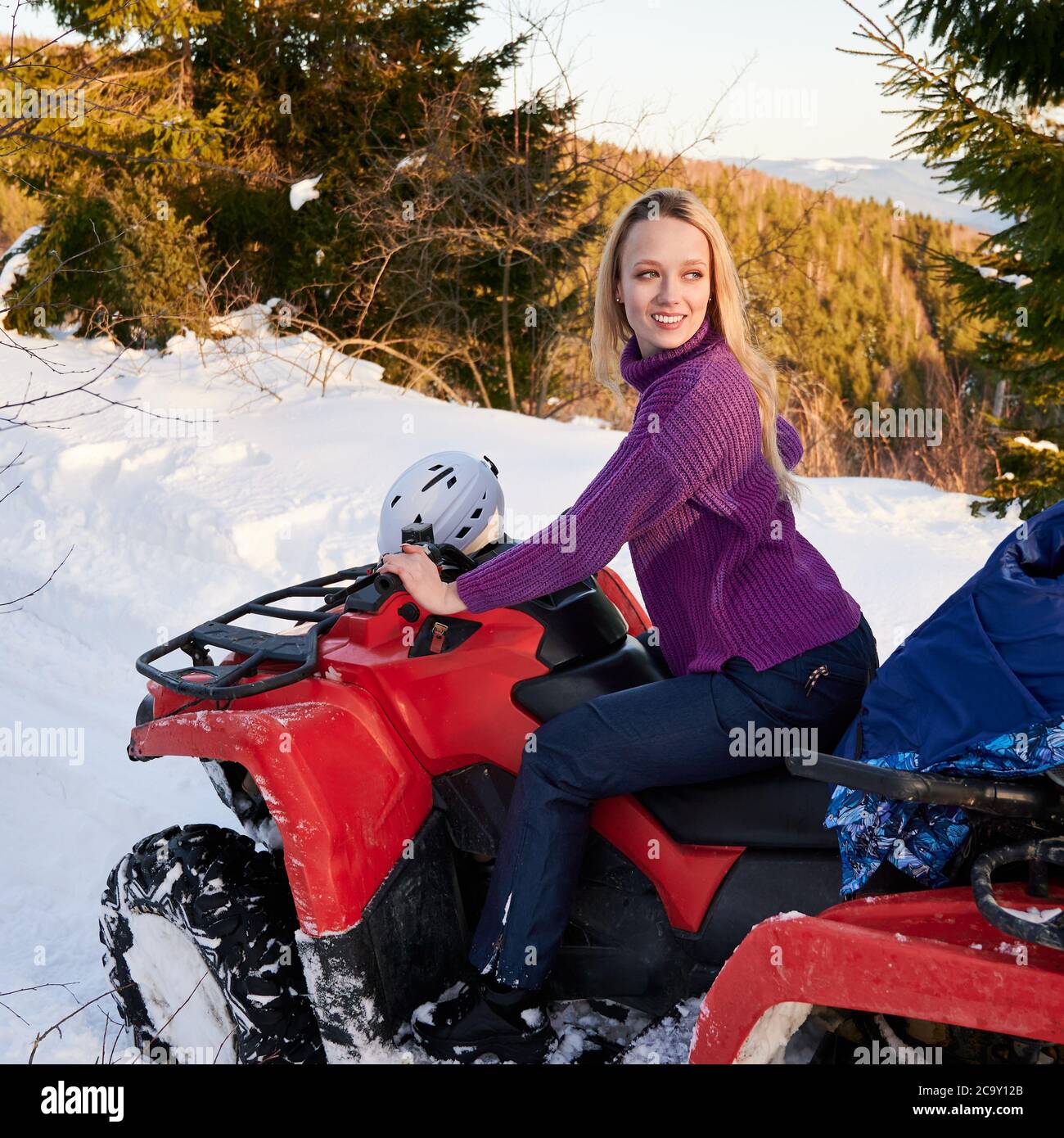 Side view of beautiful female rider in sweater sitting on red quad bike ...