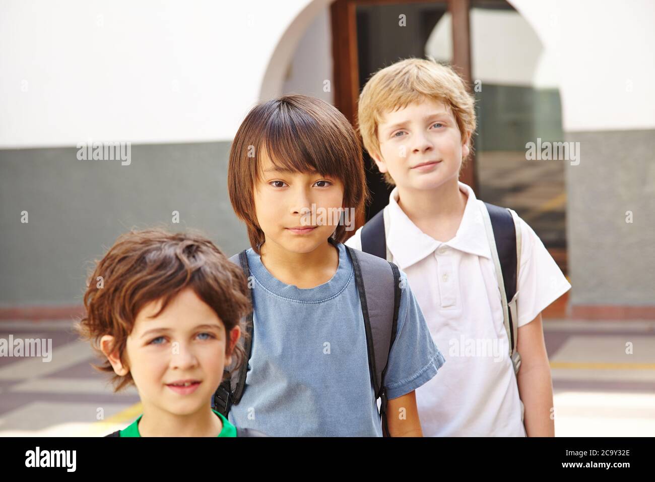 Three children stand in a row in the school yard of a primary school ...