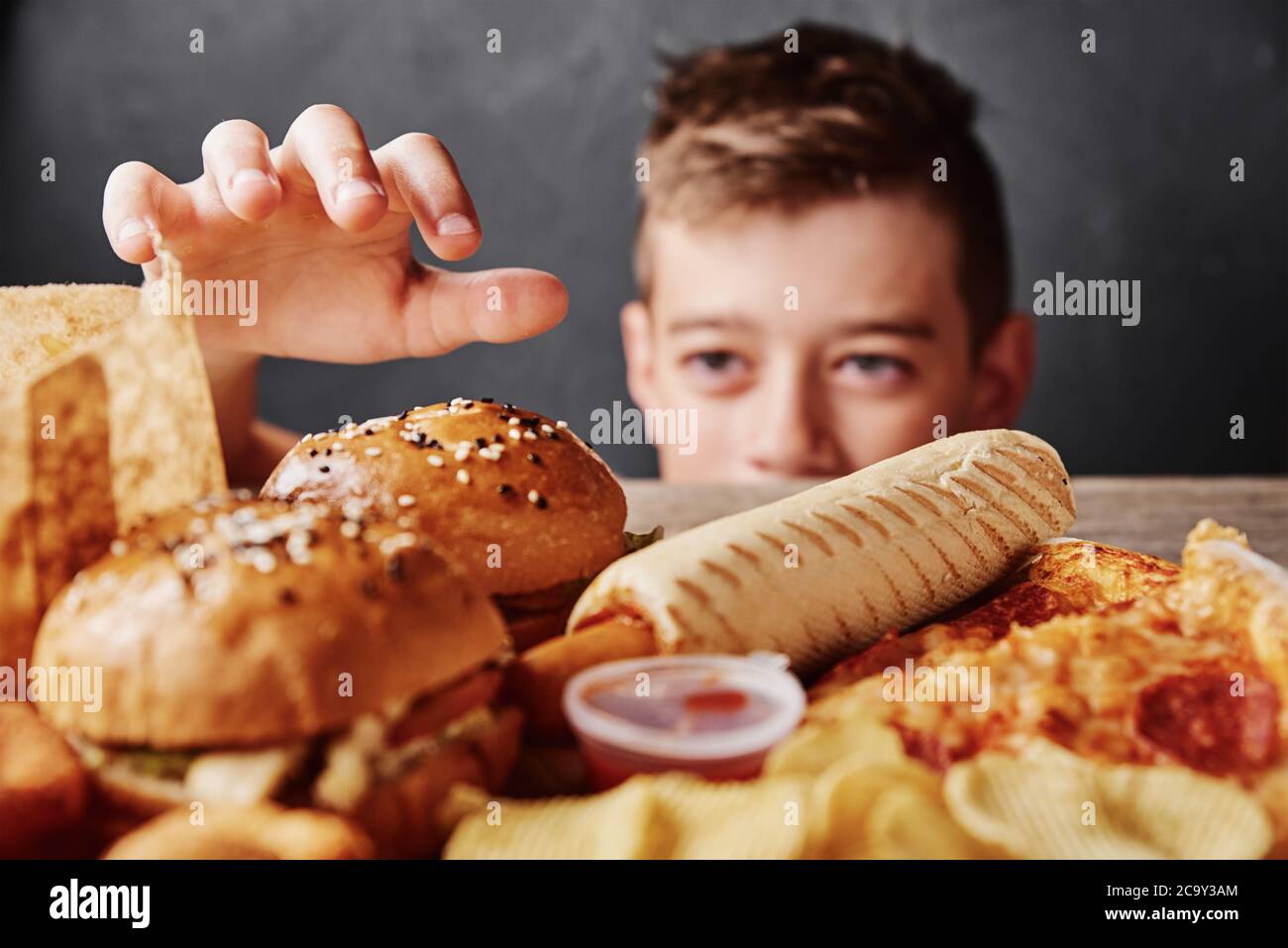 Hungry boy looks at tasty food and take hamburger from table. Unhealthy ...