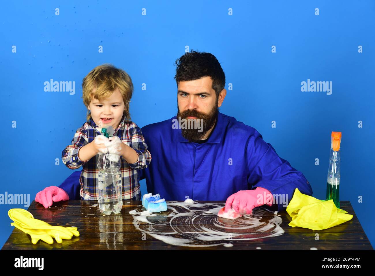 Man with strict face and exited child at wooden table on blue ...