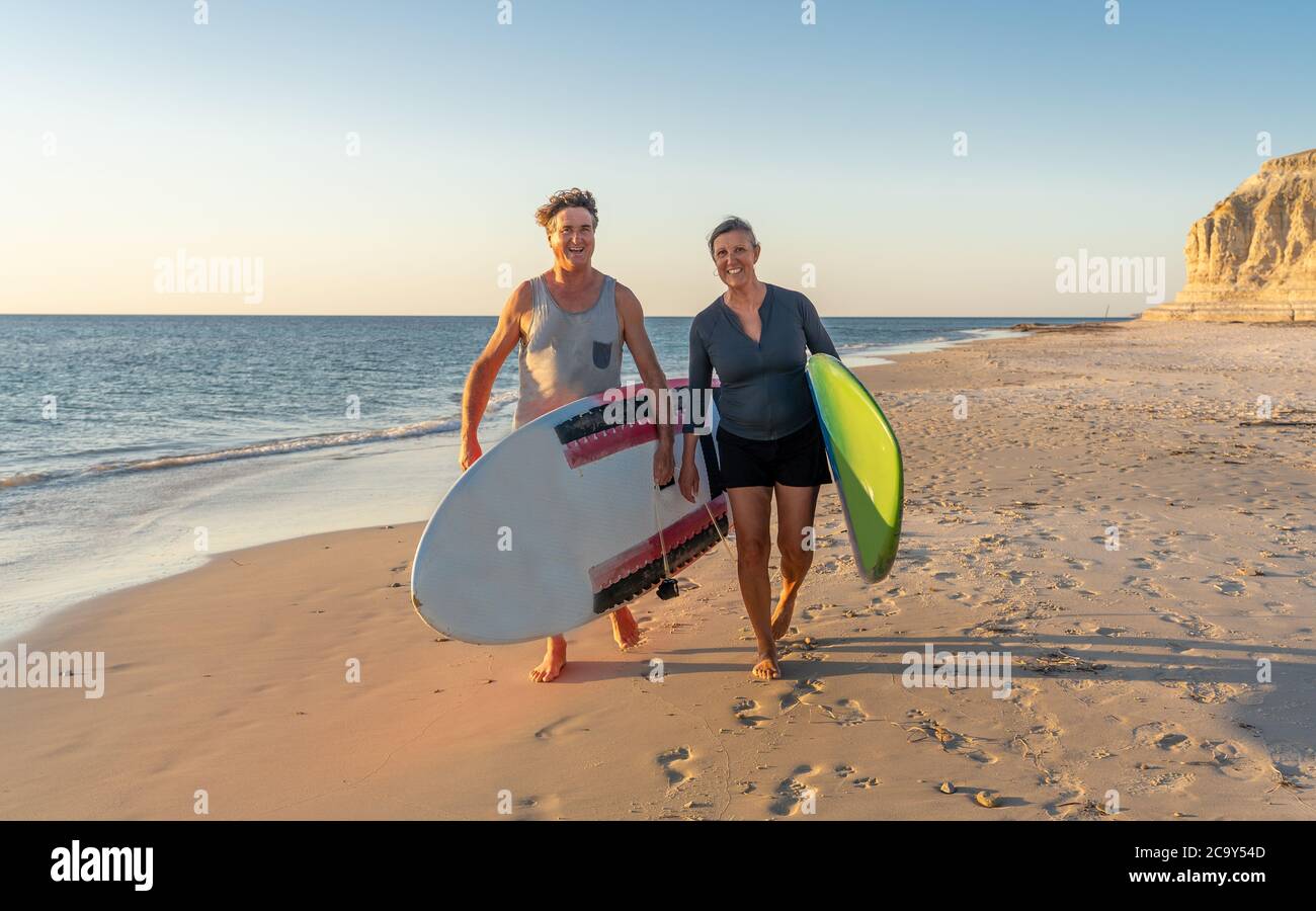 Mature couple with surfboards on beautiful beach enjoying paradise and ...