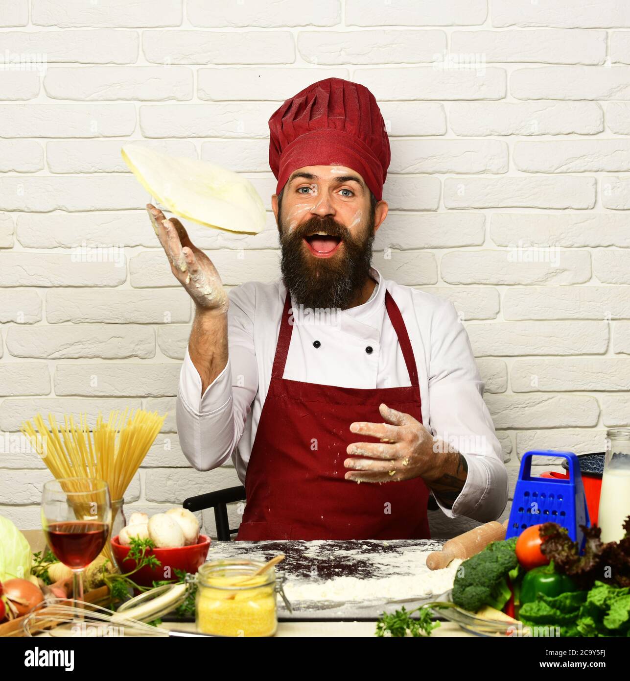 Cook with excited face in uniform sits by table with vegetables and ...