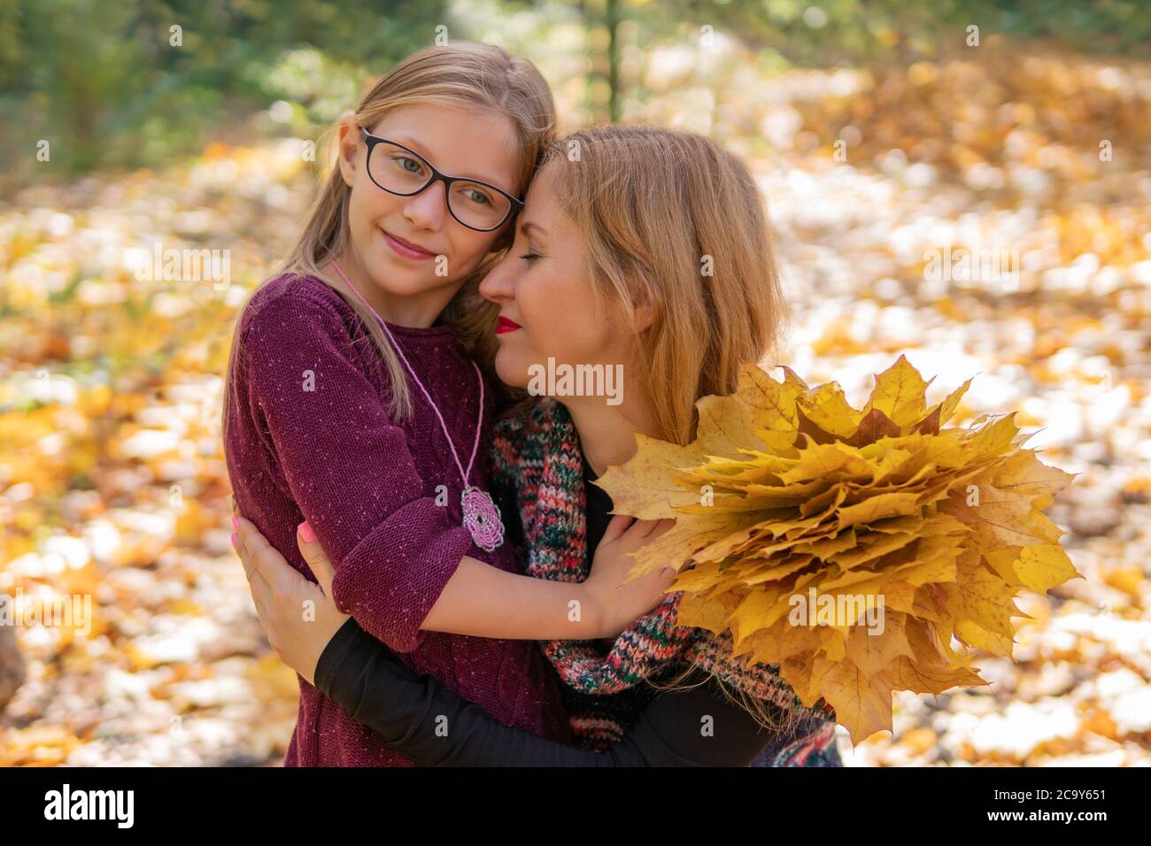 Mother lovingly hugs her daughter, with a bouquet of yellow autumn ...