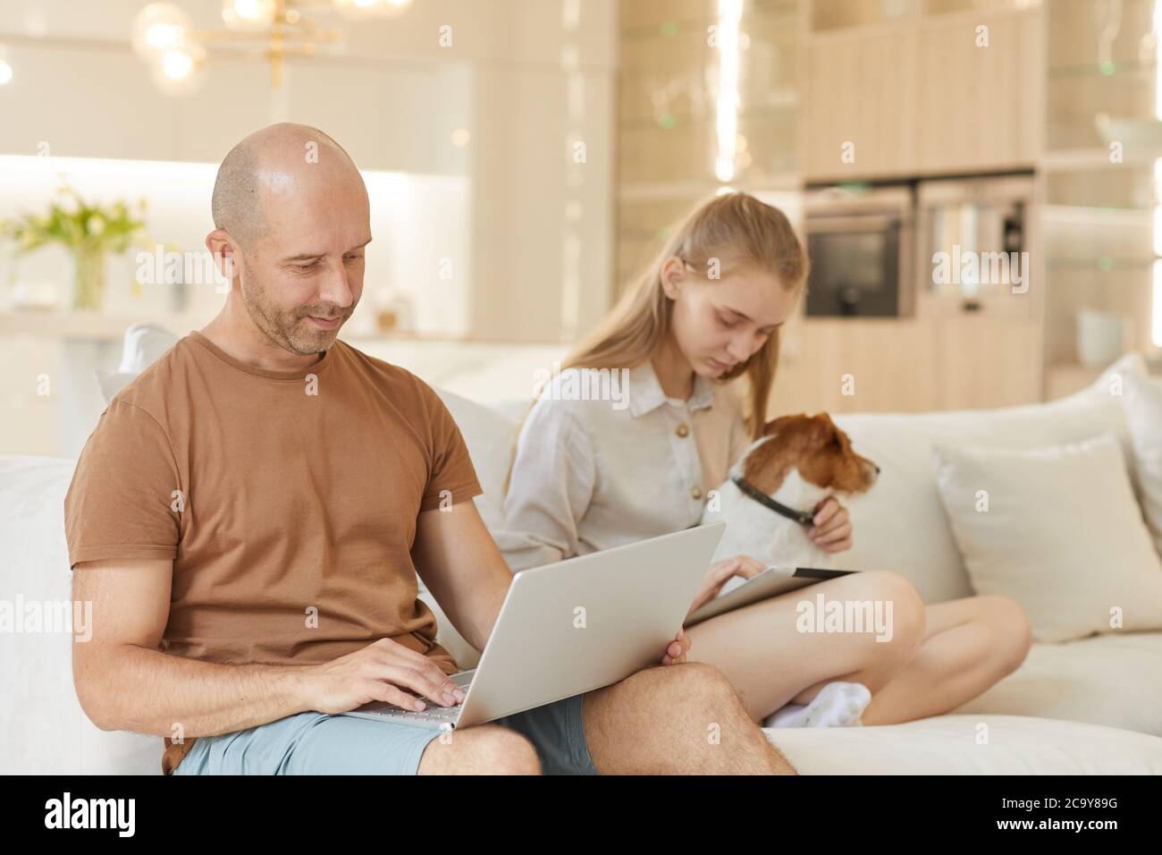 Warm-toned portrait of family using computers at home, focus on mature ...