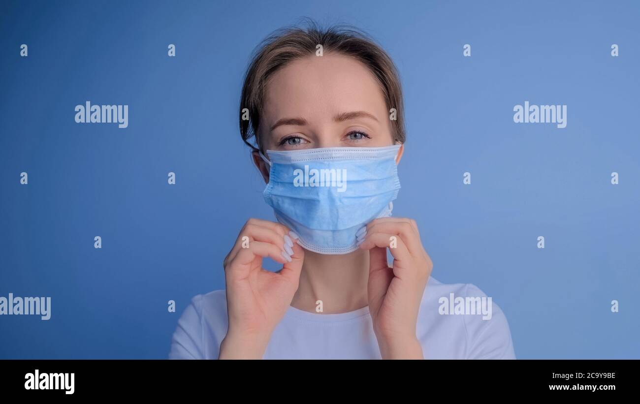 Close up: portrait of woman in white shirt putting on medical face mask ...