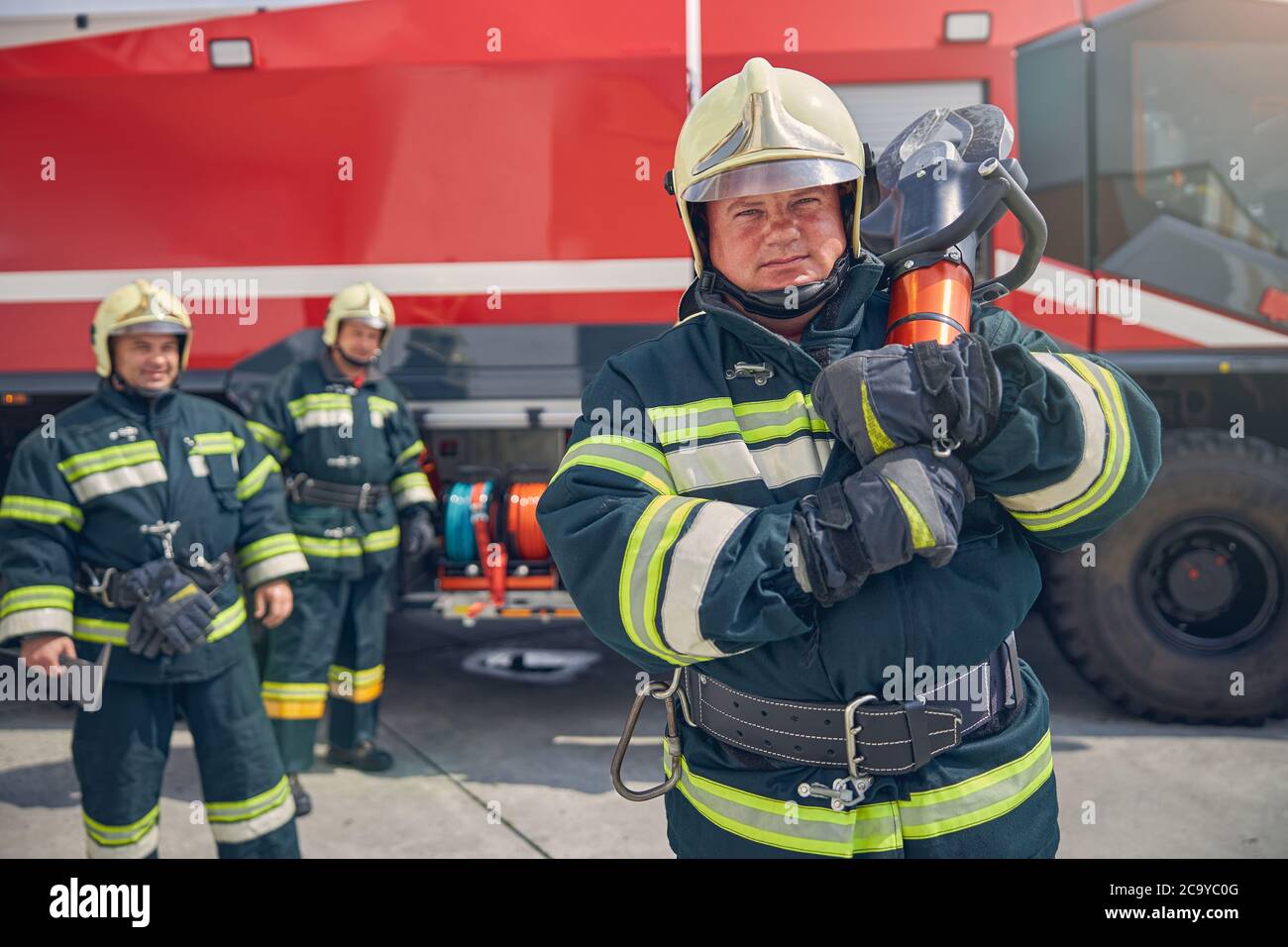 Portrait of confident fireman with male colleagues at fire station ...